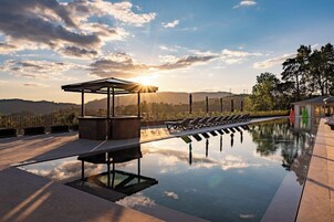 Piscina com espreguiçadeiras e uma pérgula, cercada por árvores e colinas.