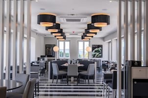 Uma zona de refeições moderna com uma mesa redonda central, pavimento riscado em preto e branco e iluminação pendente.