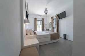 Quarto moderno com cama, mesa de cabeceira, abajur e TV fixada na parede.