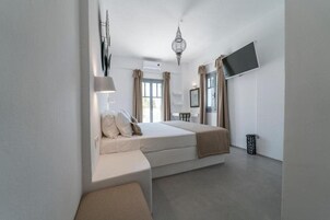 Quarto moderno com cama, mesa de cabeceira, abajur e TV fixada na parede.