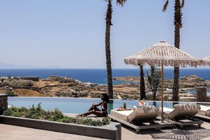 Área na piscina com espreguiçadeiras e um grande guarda-sol, com vista para uma paisagem deslumbrante e o mar.