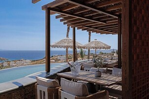 Uma área de estar externa com piscina, guarda-sóis e vista para o mar.