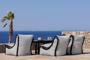 Uma área de estar com mesa e cadeiras, uma palmeira e vista para o mar.