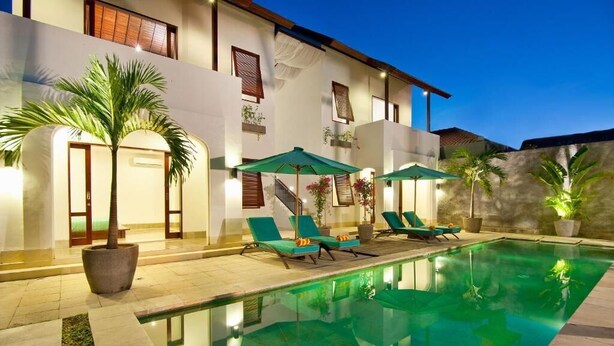 A pool area with lounge chairs and umbrellas, a building with multiple windows, and a clear sky.
