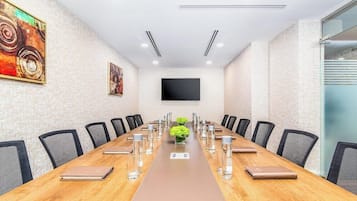 Uma sala de conferências com uma mesa comprida, cadeiras, uma TV de tela plana e um quadro na parede.