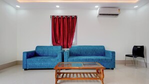 Quarto com sofá azul, mesa de centro de madeira, cadeira preta e aparelho de ar condicionado.