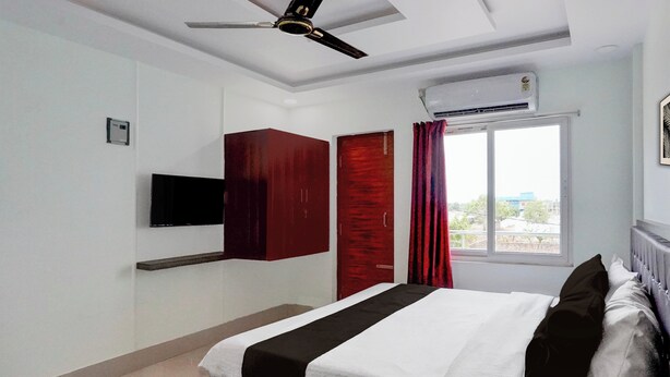 Quarto de hotel com cama, televisão, ar condicionado, guarda-roupa e janela com cortinas.