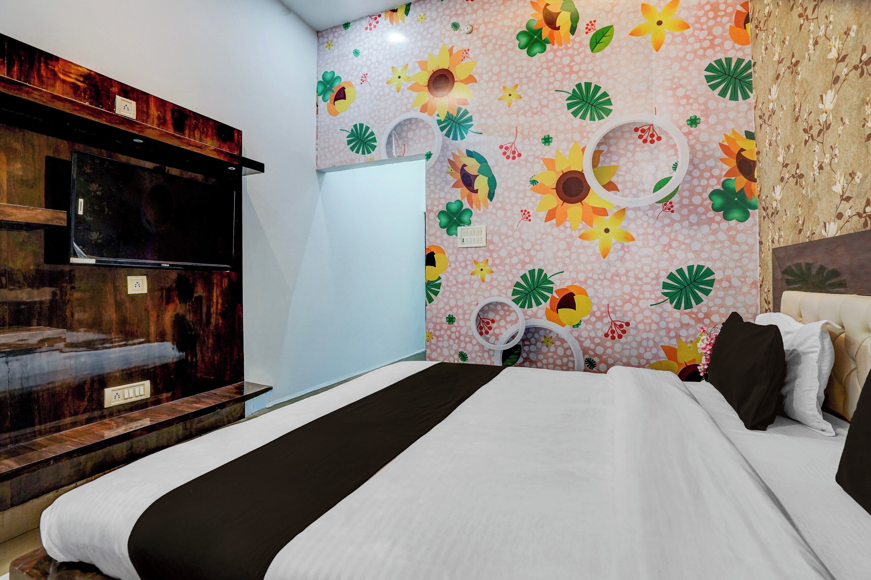 Quarto de hotel com uma cama, uma televisão e uma parede com padrão floral.