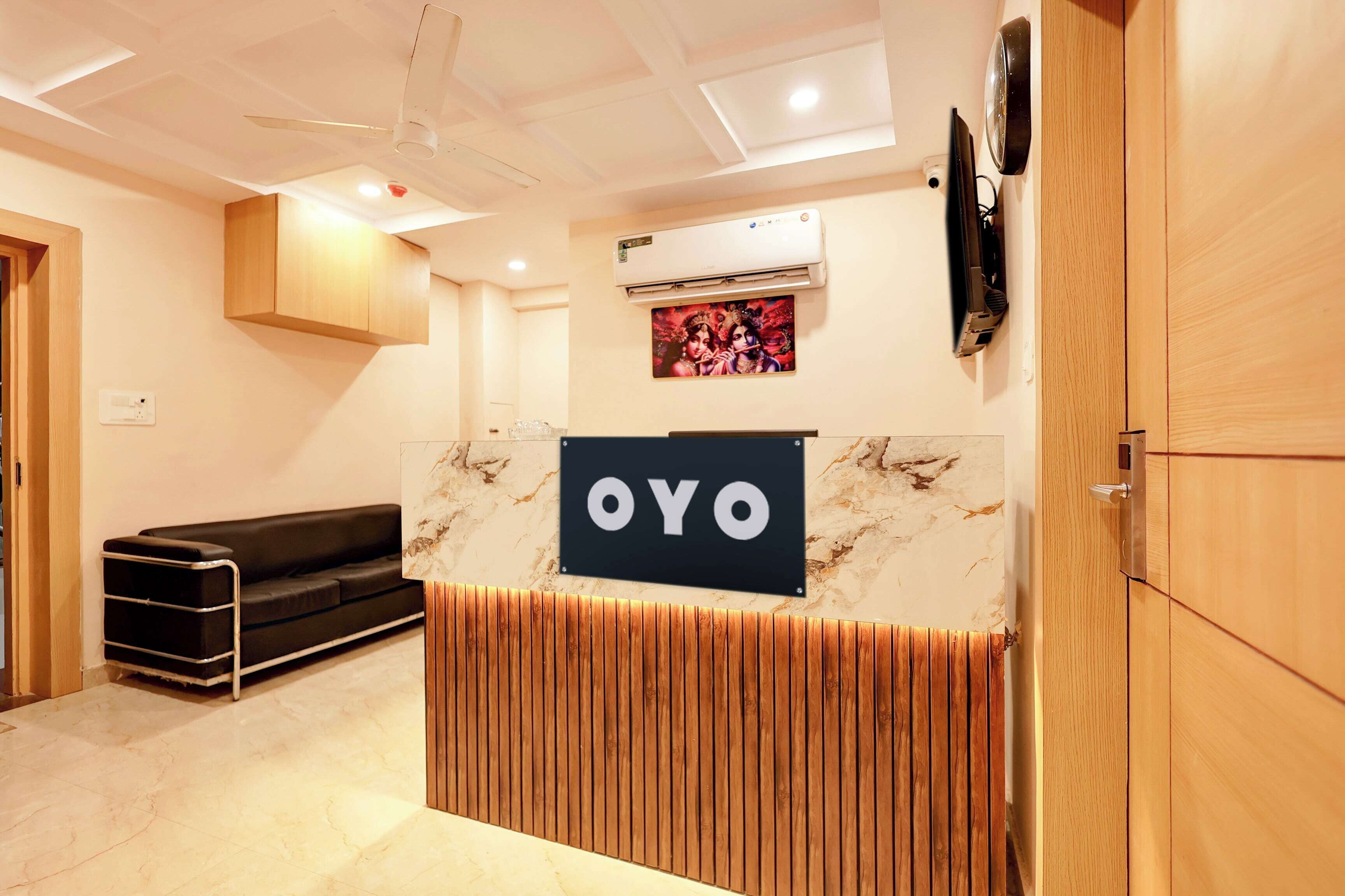 Uma receção com um letreiro a indicar 'OYO' num hall de hotel moderno, com um ventilador de teto, unidade de ar condicionado e uma televisão de ecrã plano na parede.