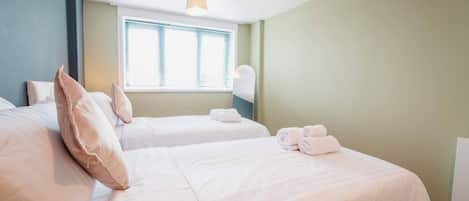 Quarto de hotel com duas camas, uma janela com persianas, uma luminária no teto e um abajur na parede.