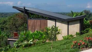 Um edifício moderno com telhado inclinado, rodeado por um jardim bem cuidado com diversas plantas e um caminho de pedra que leva à entrada.