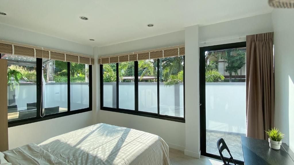 Quarto com cama, janelas amplas, porta de vidro deslizante e vista para o verde lá fora.