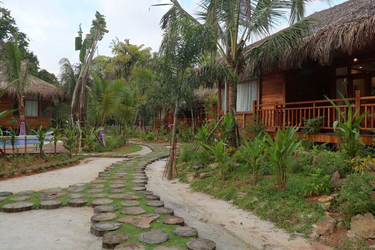 Um resort tropical com cabanas de telhado de palha, um caminho pavimentado e vegetação exuberante.