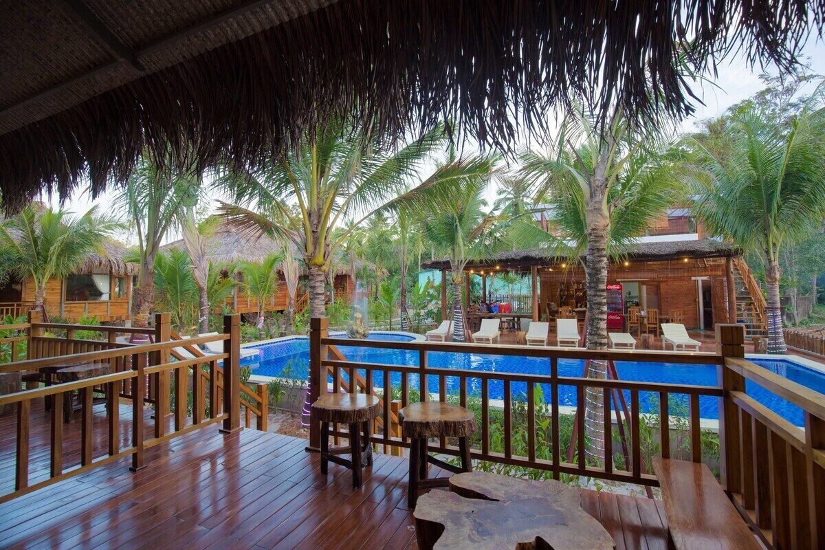 Um deck de madeira com piscina, cadeiras de descanso e área de bar.
