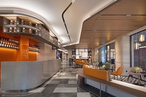 Um lobby de hotel moderno com área de bar, assentos e vista para a cidade.