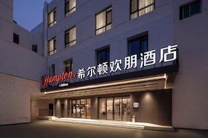 Exterior de hotel com uma placa indicando 'Hampton by Hilton' e caracteres chineses.
