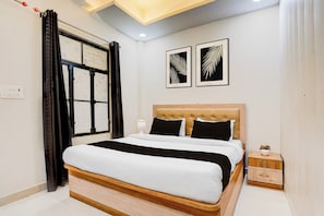 Quarto de hotel com cama, mesa de cabeceira, abajur e duas obras de arte emolduradas na parede.