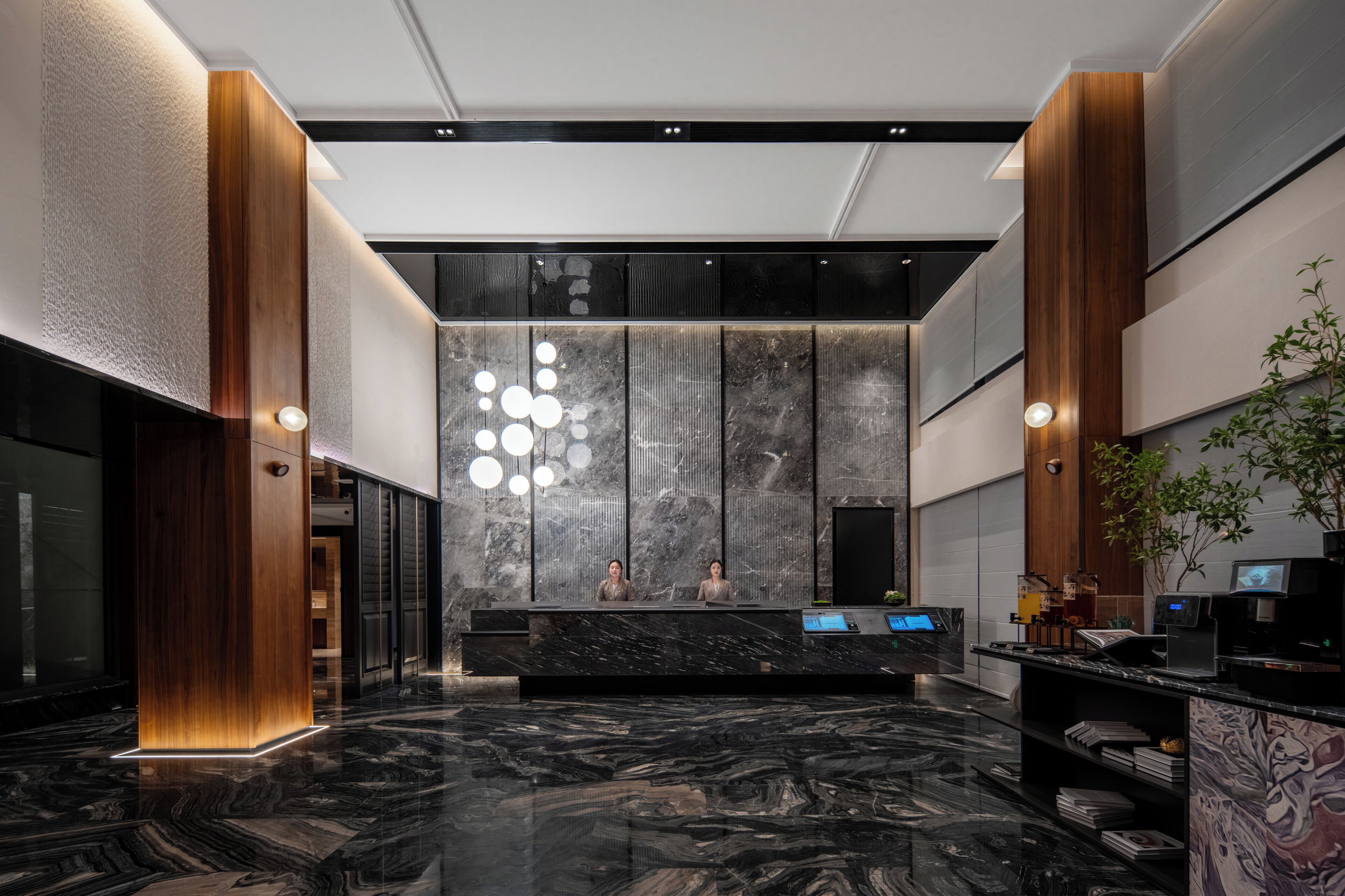 Uma área de recepção moderna com piso de mármore, balcão de recepção e uma parede grande com luminária geométrica.