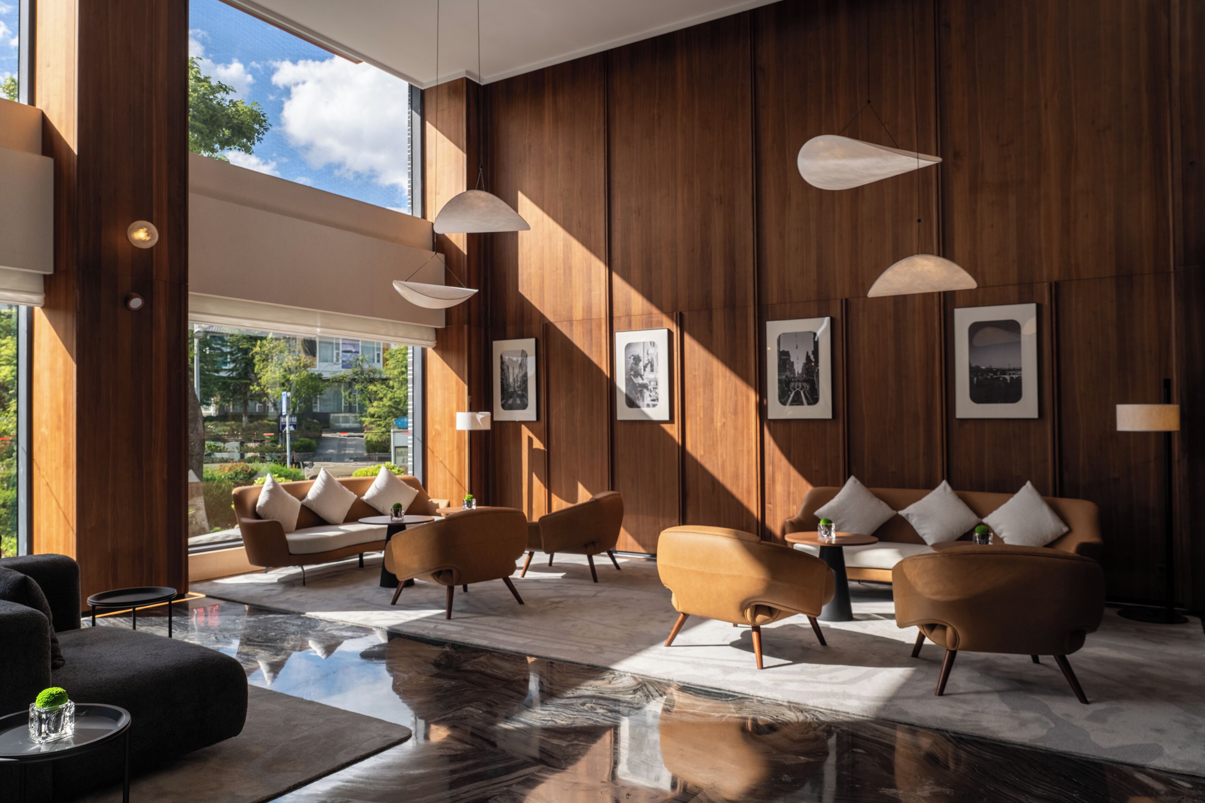 Um lobby moderno com painéis de madeira, piso de mármore e uma área de estar com sofás e poltronas.