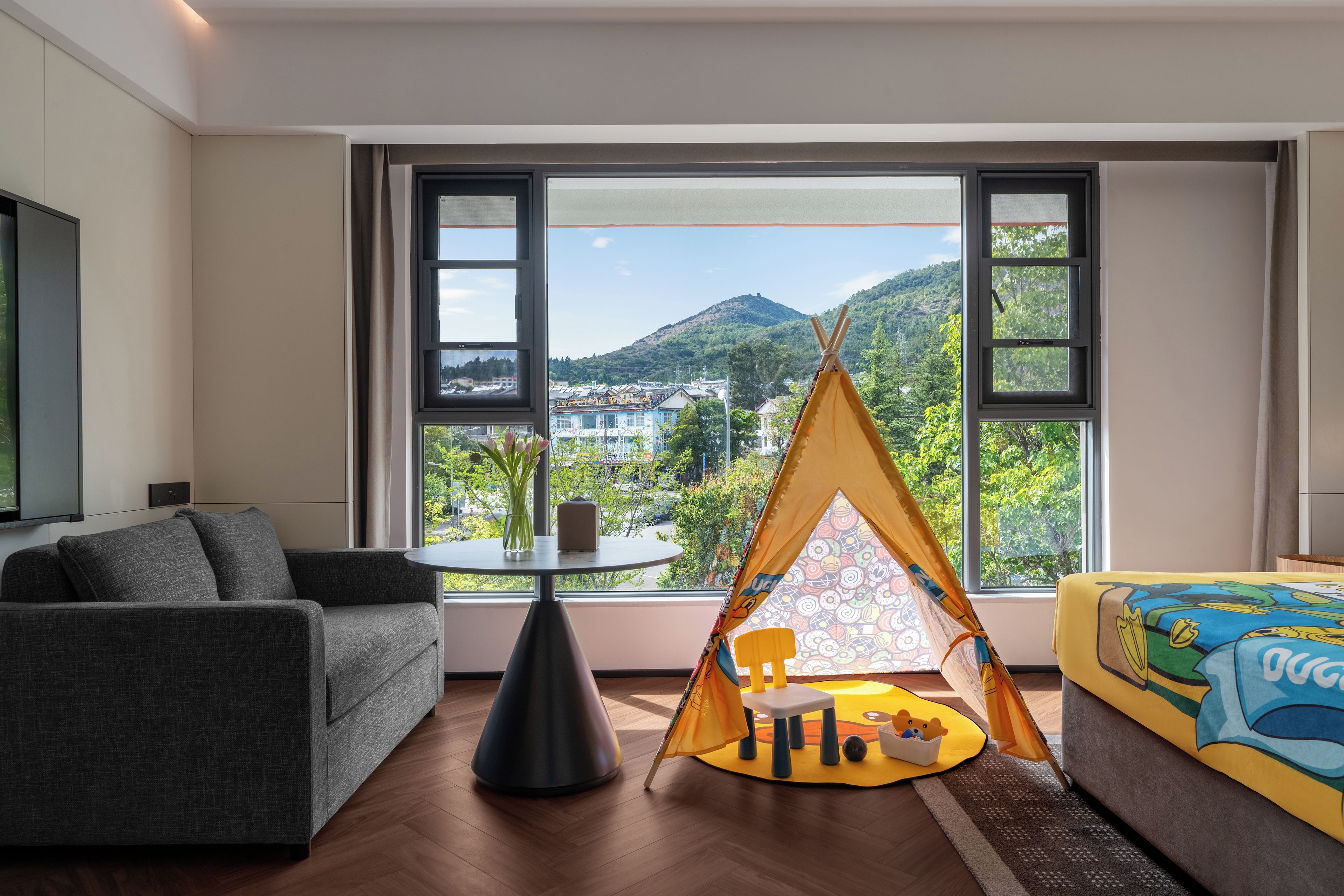 Uma sala de estar moderna com sofá, mesa com um vaso, uma tenda e uma cama com um cobertor colorido.