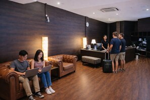 Um saguão de hotel com sofás de couro, um balcão de recepção e um carrinho de bagagem.