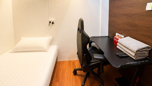 Quarto de hotel com cama, escrivaninha com cadeira, controle remoto e uma pilha de toalhas.