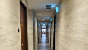 Um corredor comprido e estreito, com paredes de mármore e chão de azulejos, que termina numa porta.