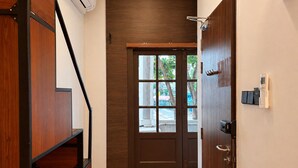 Um corredor com uma porta de madeira, uma janela com vista para a rua e um telefone fixado na parede.