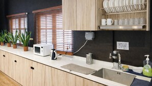 Uma cozinha moderna com armários de madeira, micro-ondas, chaleira, pia e escorredor de louça.
