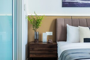 Quarto de hotel com uma cama, uma mesa de cabeceira com uma planta, uma xícara e uma tomada.