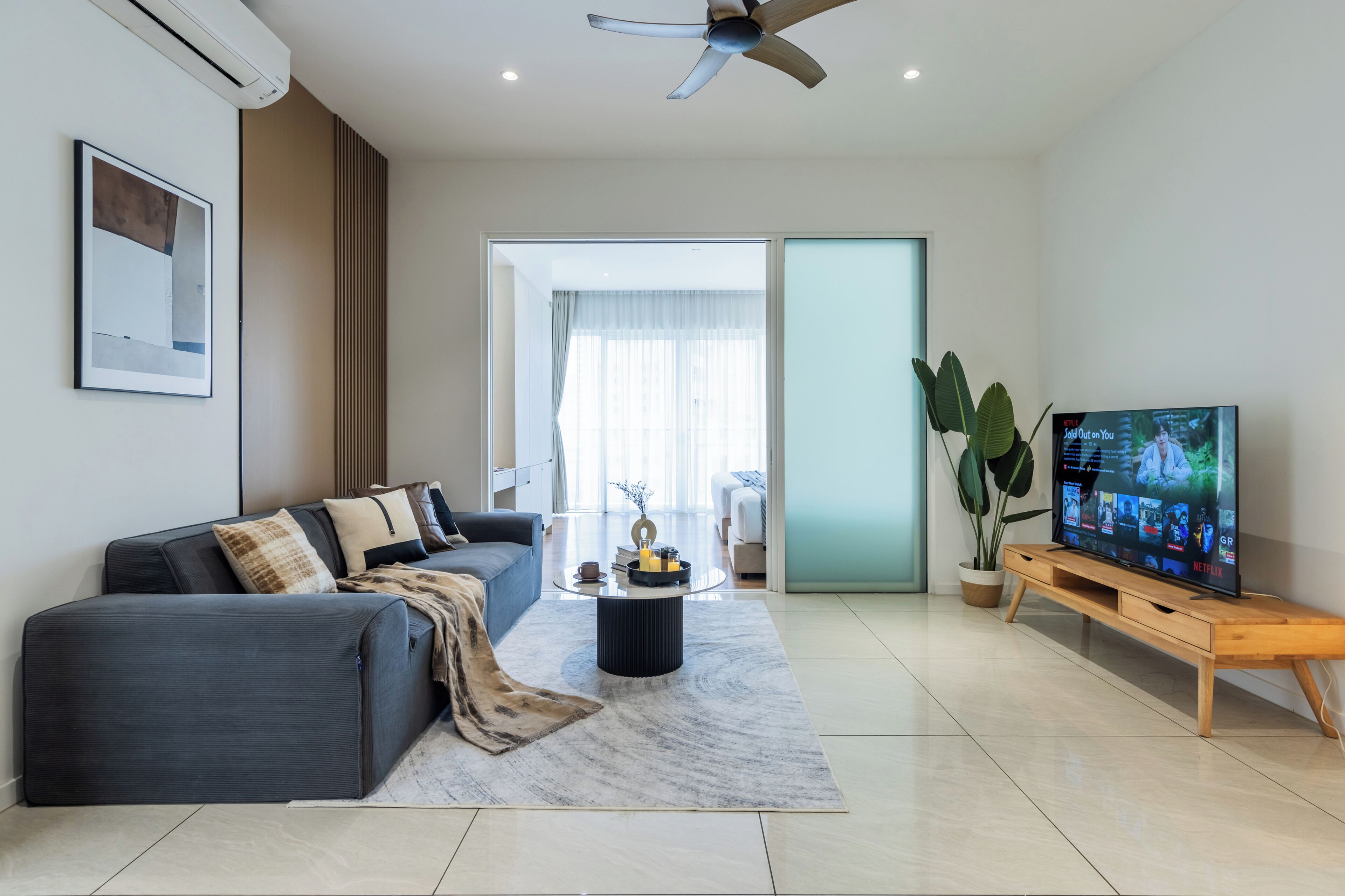 Uma sala de estar moderna com um sofá, mesa de centro e uma televisão sobre um suporte de madeira.