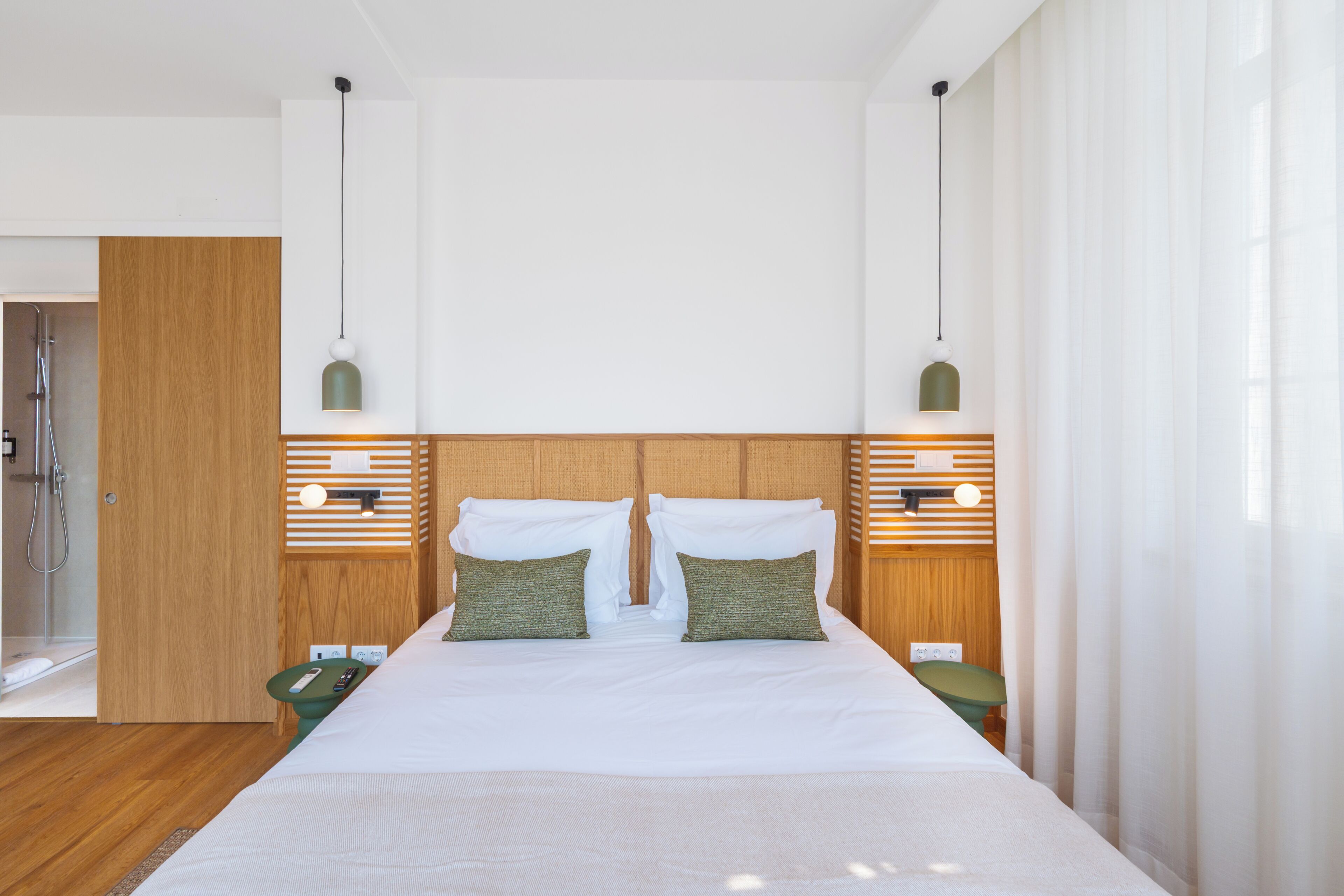 Quarto de hotel moderno com uma cama grande, cabeceira de madeira e duas mesas de cabeceira com luminárias.