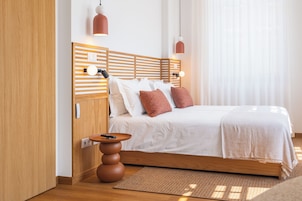 Quarto moderno com cabeceira de madeira, mesa de cabeceira com um controle remoto e uma janela grande com cortinas leves.