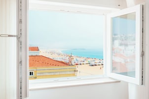 Janela com vista para uma praia com guarda-sóis e edifícios.