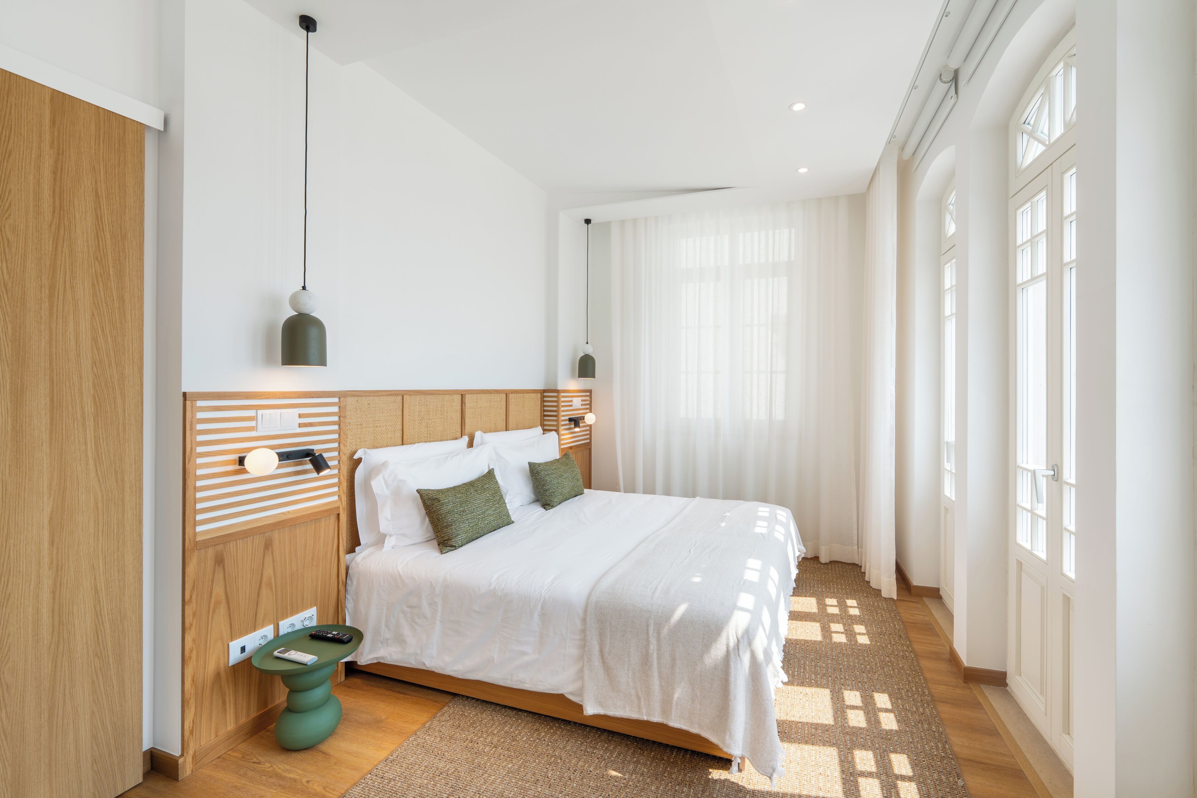Um quarto moderno com cabeceira de madeira, cama com roupa de cama branca e uma pequena mesa de cabeceira com um controle remoto.