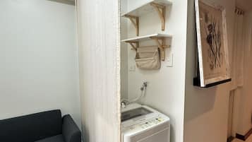 Quarto compacto com máquina de lavar, sofá e cortina.