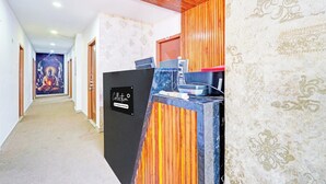 Corredor de hotel com uma mesa de recepção, parede com padrão floral e corredor com um mural.