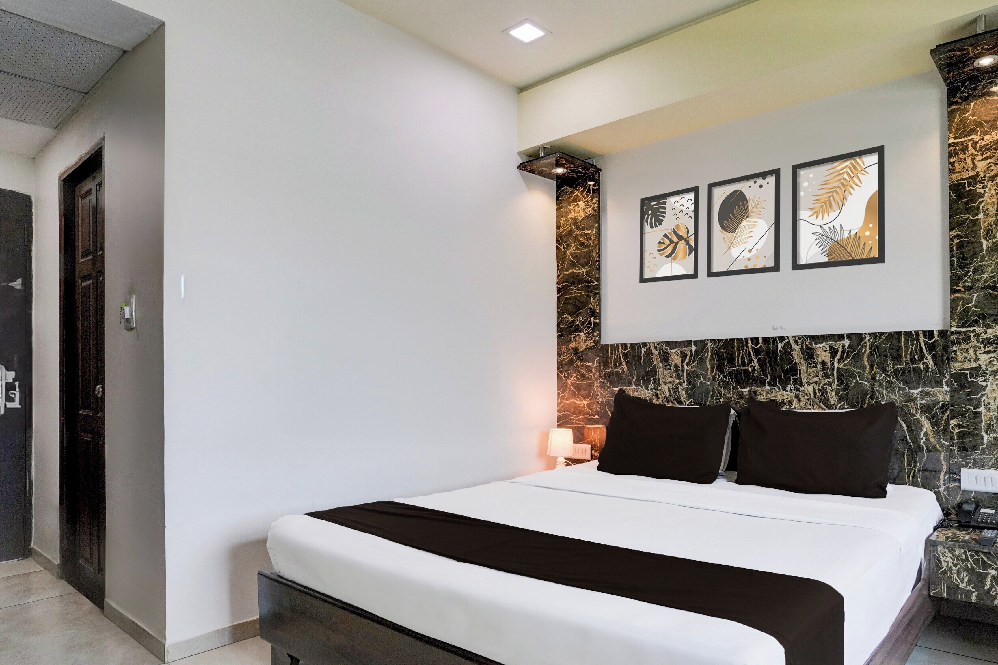 Quarto de hotel com cama, mesa de cabeceira, luminária na parede e obras de arte emolduradas.