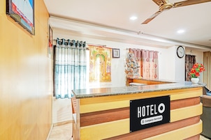 Balcão de recepção de hotel com placa indicando serviço da empresa. Cortinas, um relógio e um ventilador de teto são visíveis.