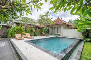 Uma piscina com espreguiçadeiras e uma pequena casa com telhado em azulejos.