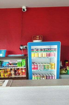 Uma máquina de vendas com diversas bebidas e petiscos, uma câmera de segurança na parede e uma placa com caracteres chineses.