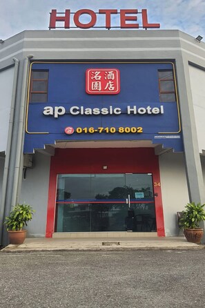 Um hotel com uma placa grande 'HOTEL' no topo, fachada em vermelho e azul e um número de contato exibido abaixo.