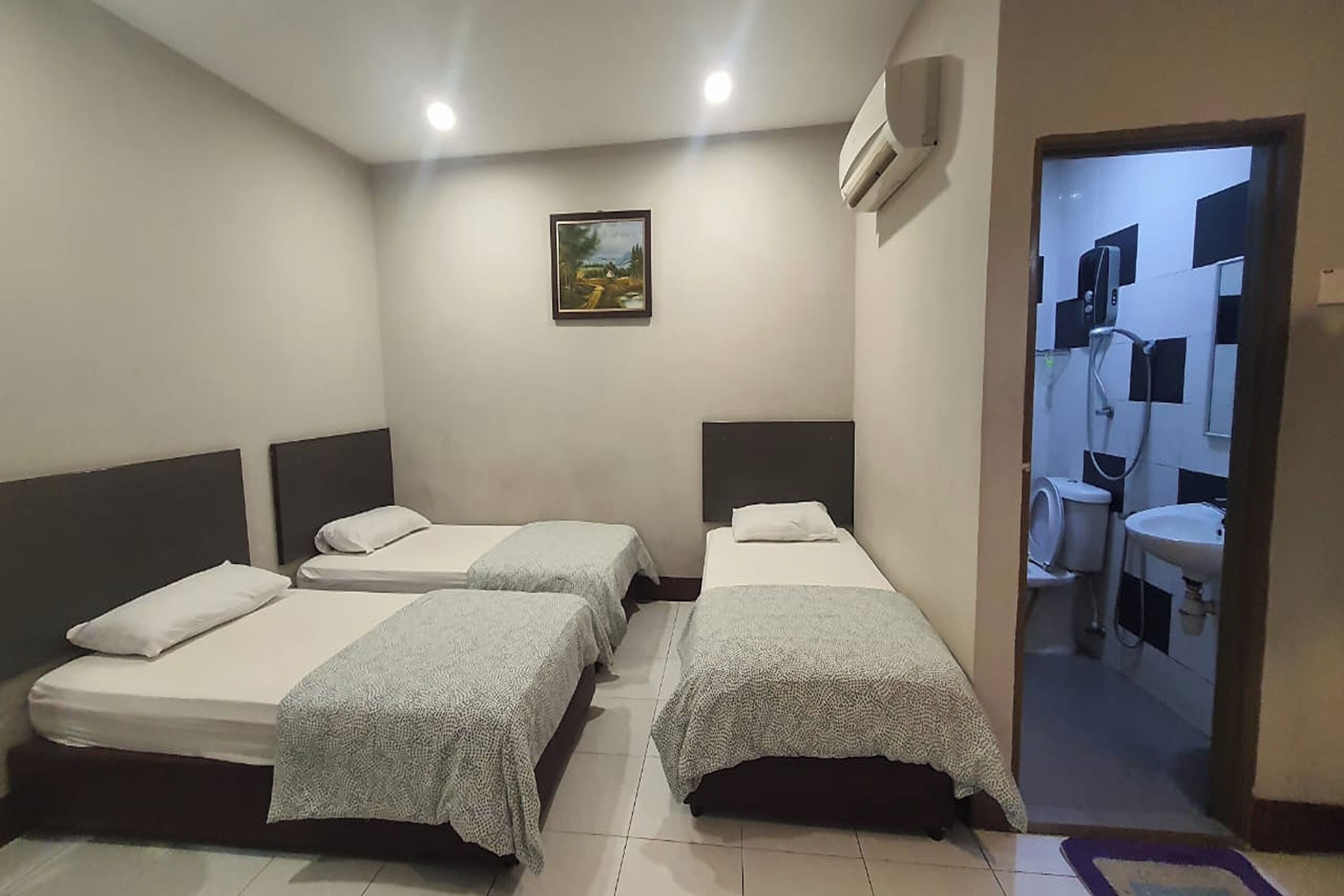 Quarto de hotel com duas camas, um pequeno quadro na parede e um banheiro visível através de uma porta aberta.