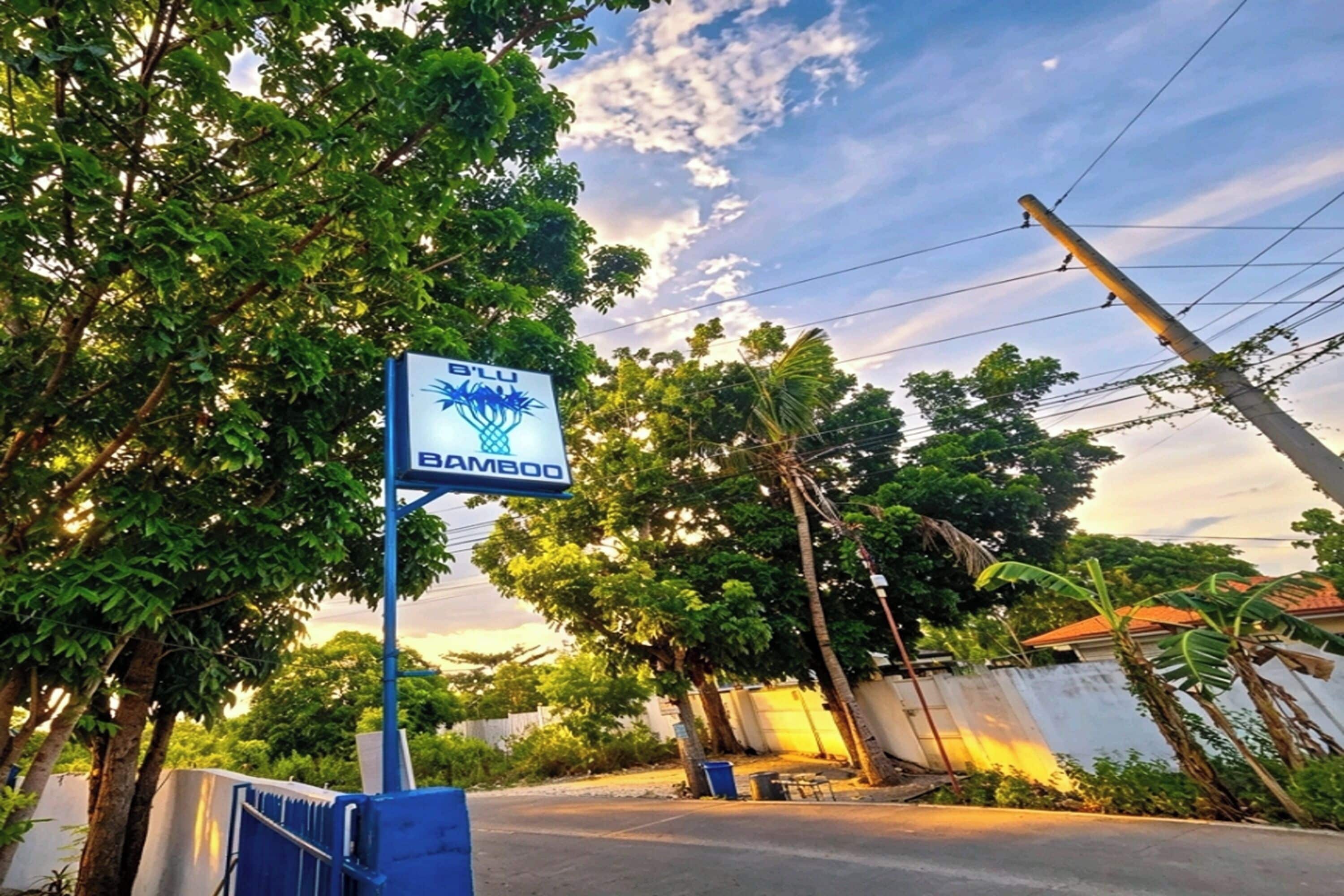 A street sign with 'B'LU BAMBOO' written on it, surrounded by lush greenery and a clear sky.