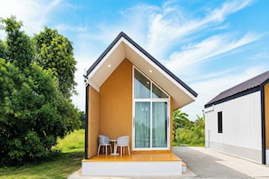 Uma casa moderna com uma grande porta de vidro, um pequeno alpendre com duas cadeiras e um jardim bem cuidado.