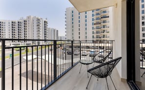 Varanda com mesa e cadeiras, com vista para uma rua com carros e edifícios.