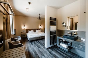 Quarto de hotel moderno com cama, mesas de cabeceira, um banco embutido, uma toucador com espelho e uma pequena janela.