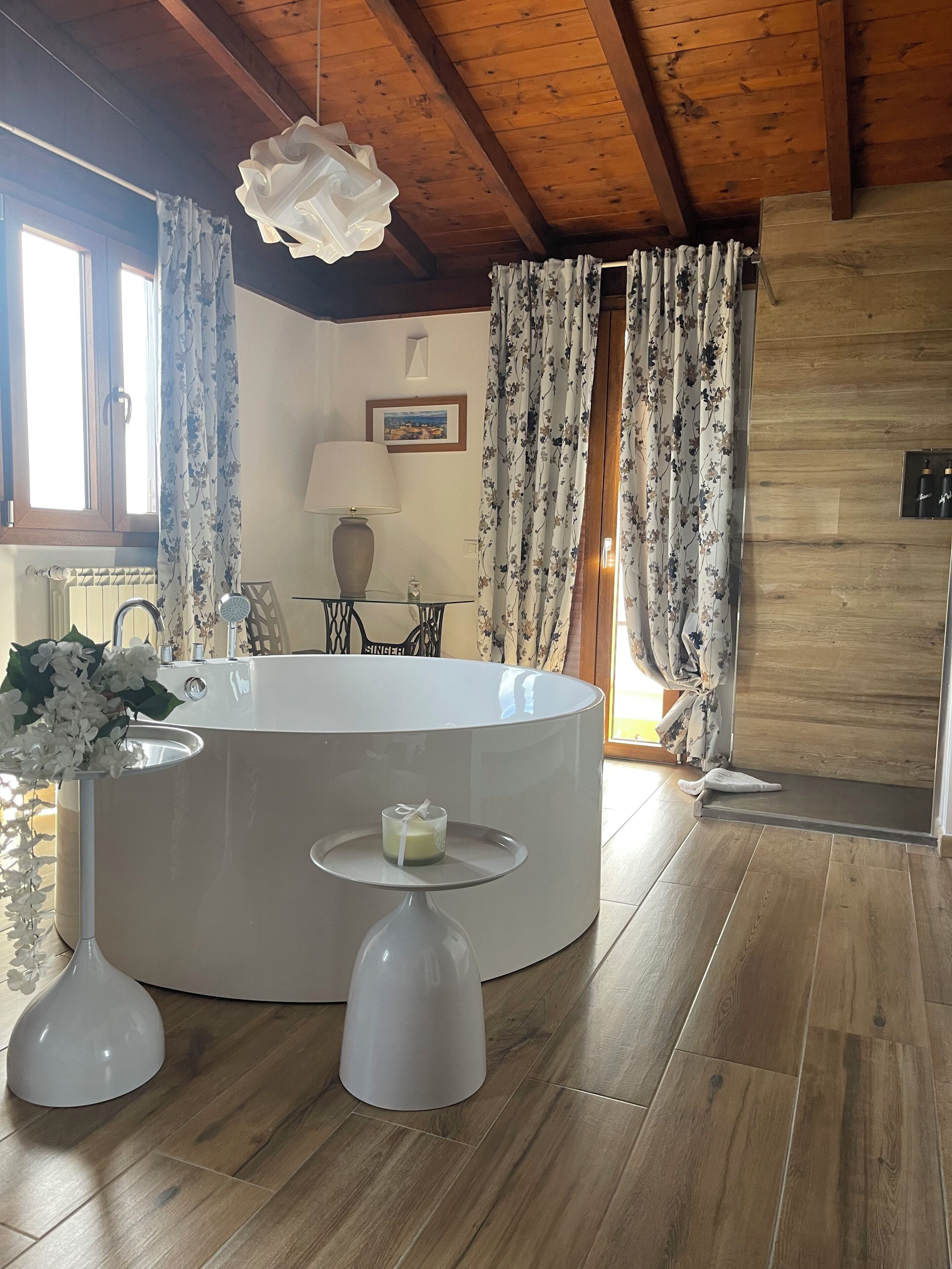 Uma casa de banho moderna com uma banheira independente, uma mesa de vidro com uma vela e soalho em madeira.