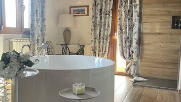 Uma casa de banho moderna com uma banheira independente, uma mesa de vidro com uma vela e soalho em madeira.