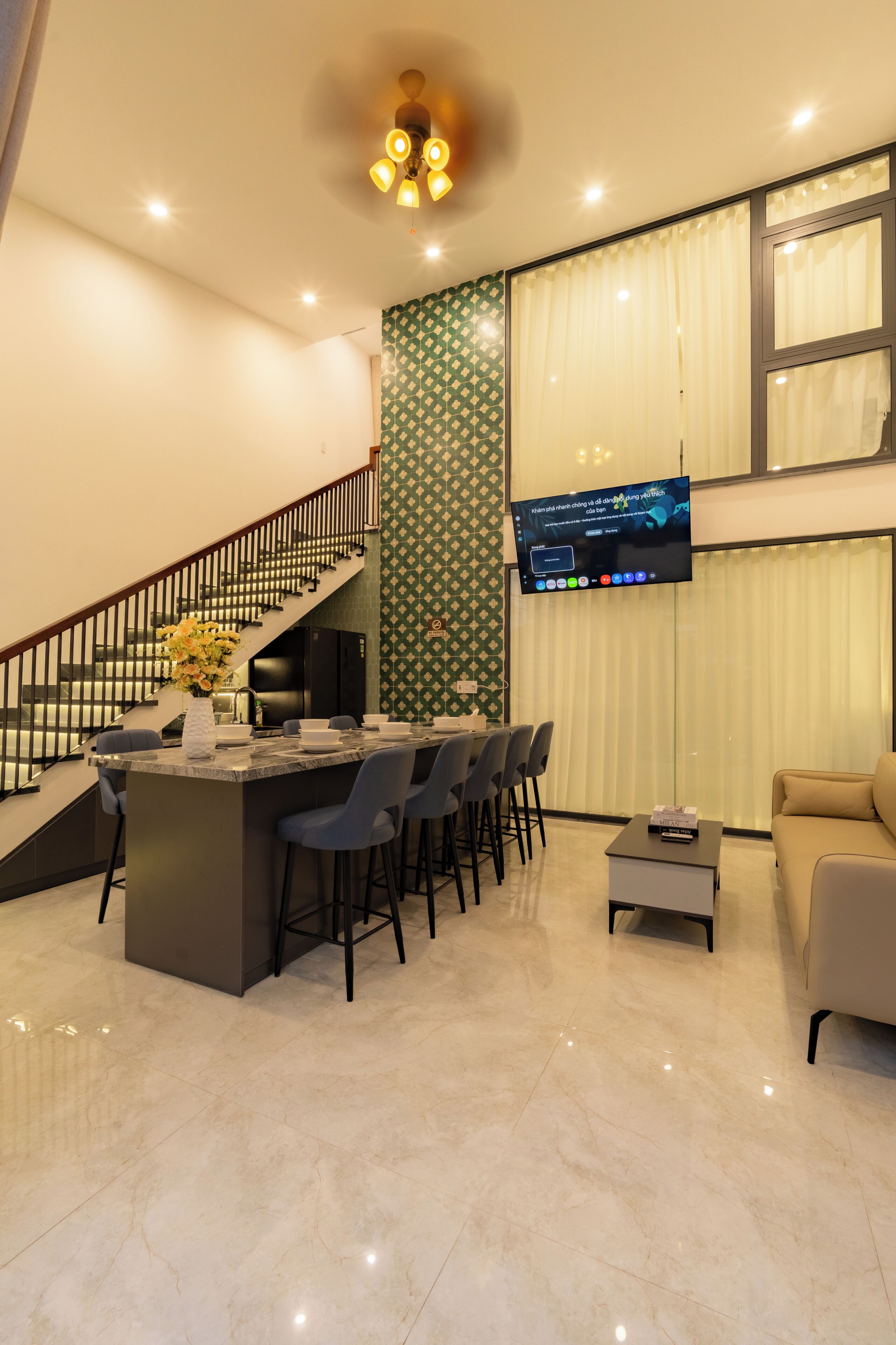Uma cozinha moderna com ilha central, banquetas, área de refeições com sofá e uma escada.